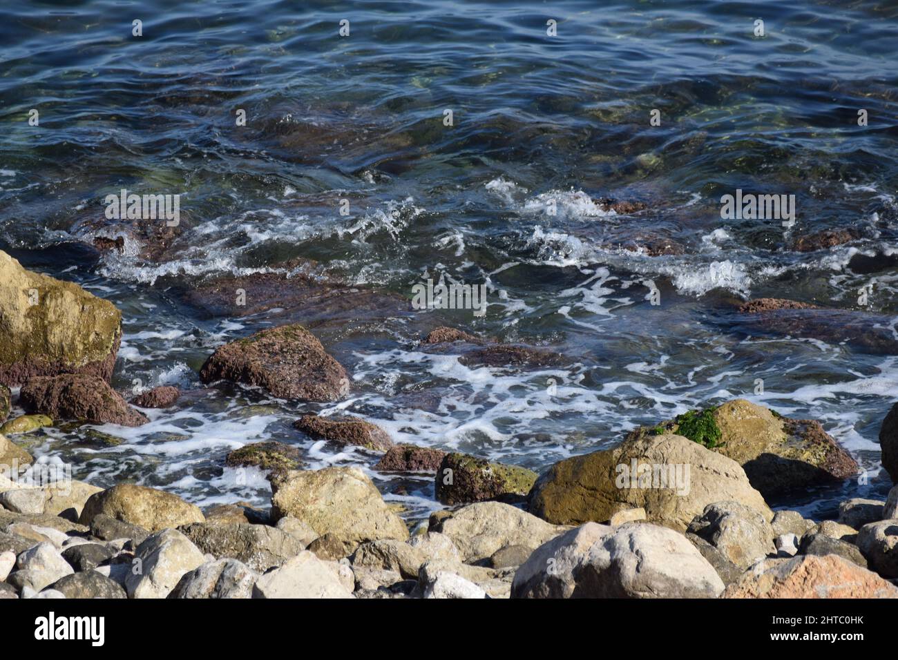 Bright summer day with the ocean water splashing around on the rocks ...