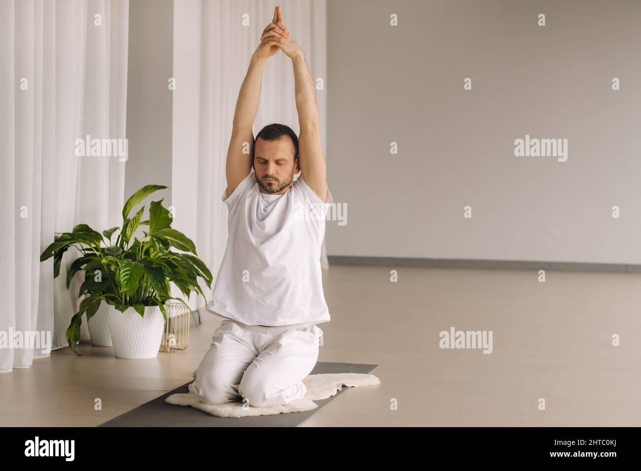 a man in white sportswear is doing yoga with a fitness room. the ...