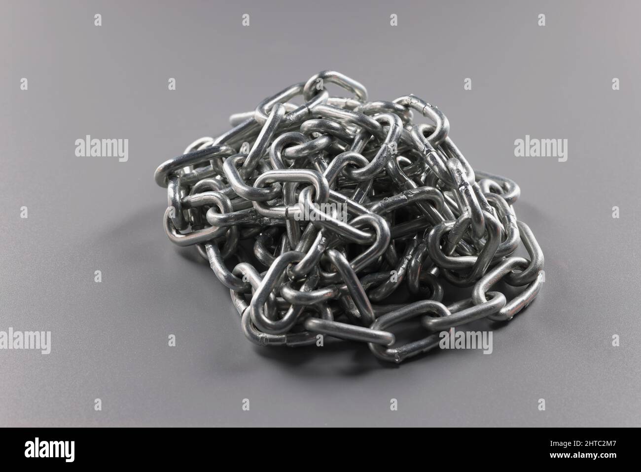 Grey solid chain folded in heap, steel metal iron chain on grey surface ...
