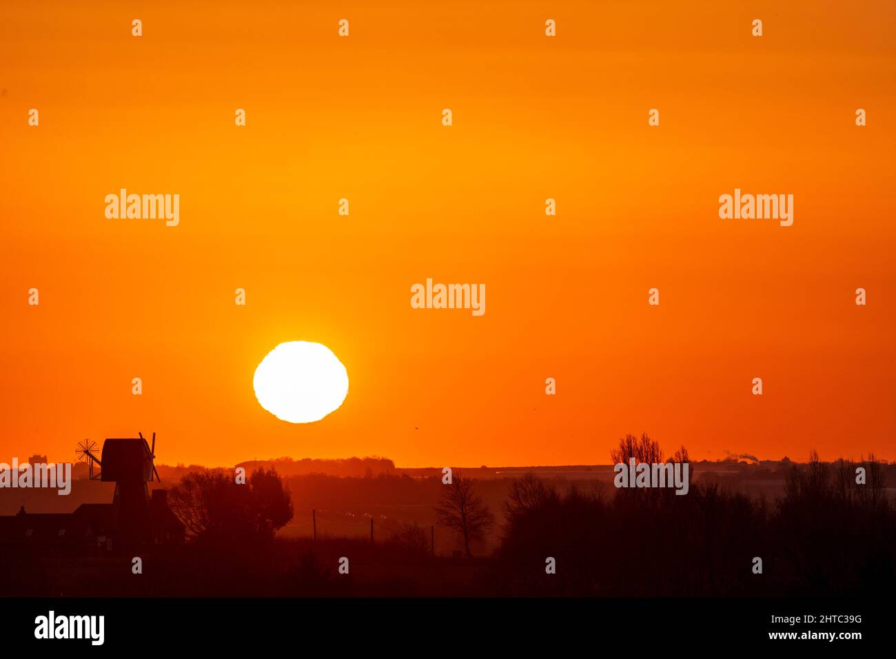 Sunrise in to a clear orange sky over a landscape of hedgerows and ...