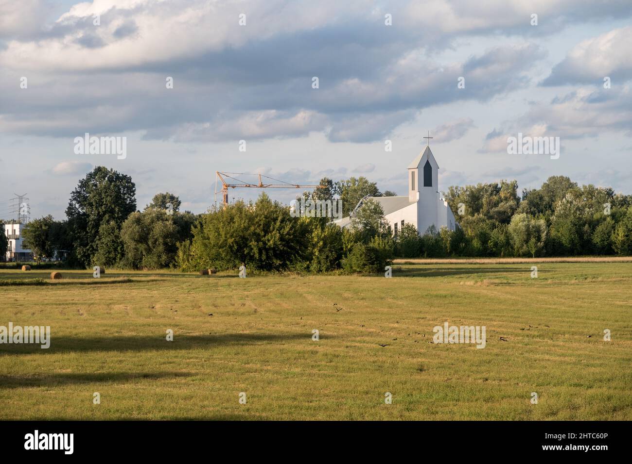 White church surrounded by field and green trees under a cloudy sky ...