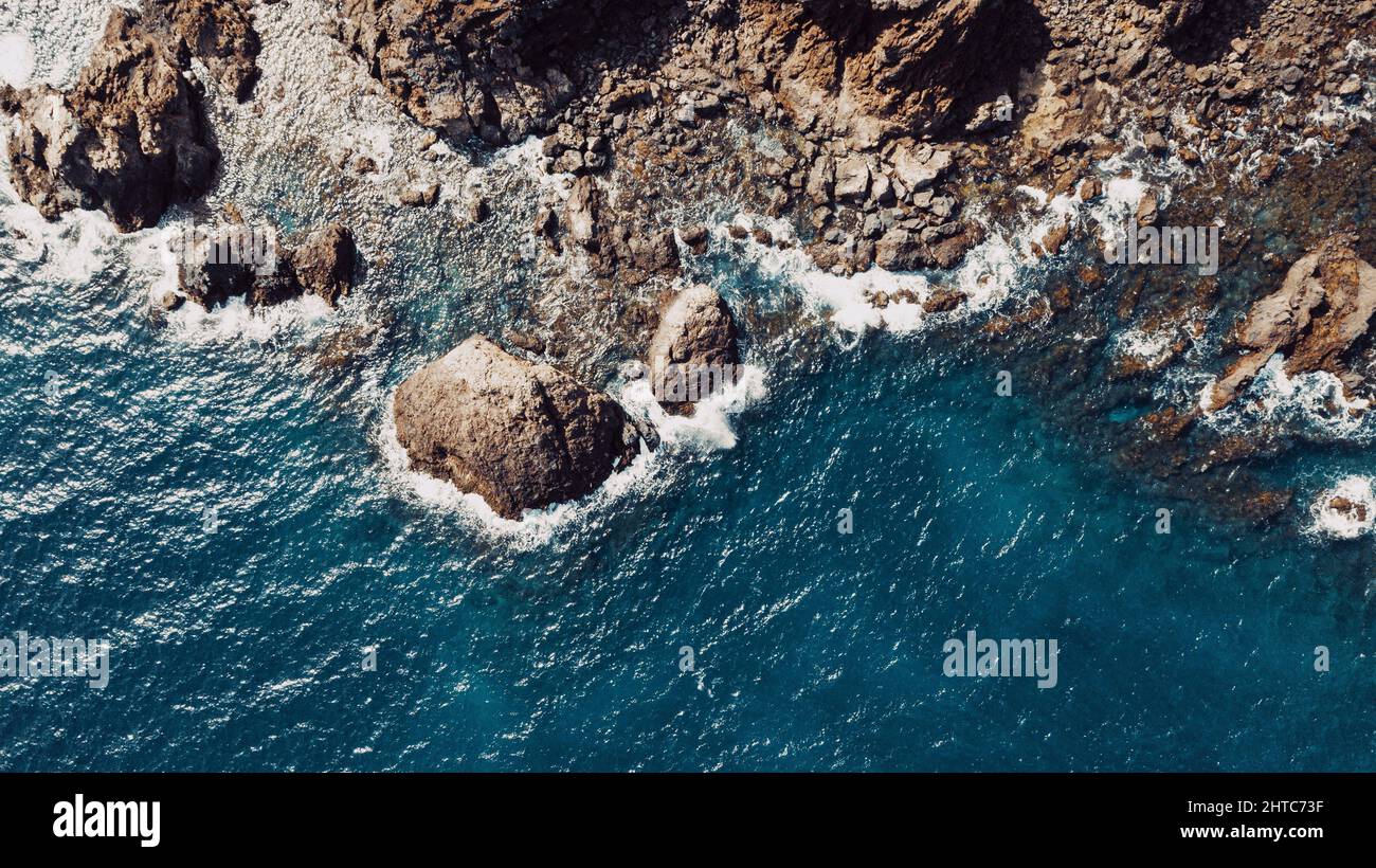 Aerial top view of waves break on rocks in a blue ocean. Sea waves on ...