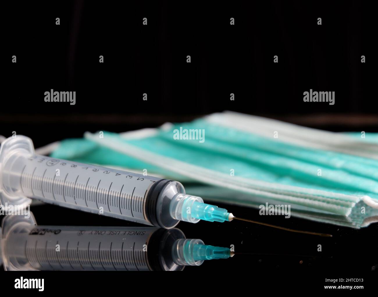 Closeup of a syringe with a needle near a face mask on a reflective ...