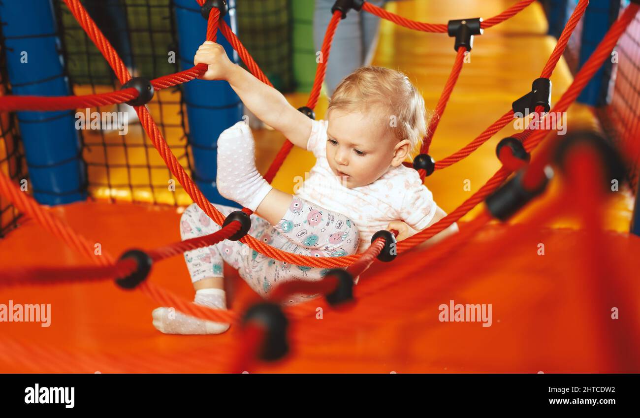 Excited little girl playing on net ropes at amusement park. Cute baby ...