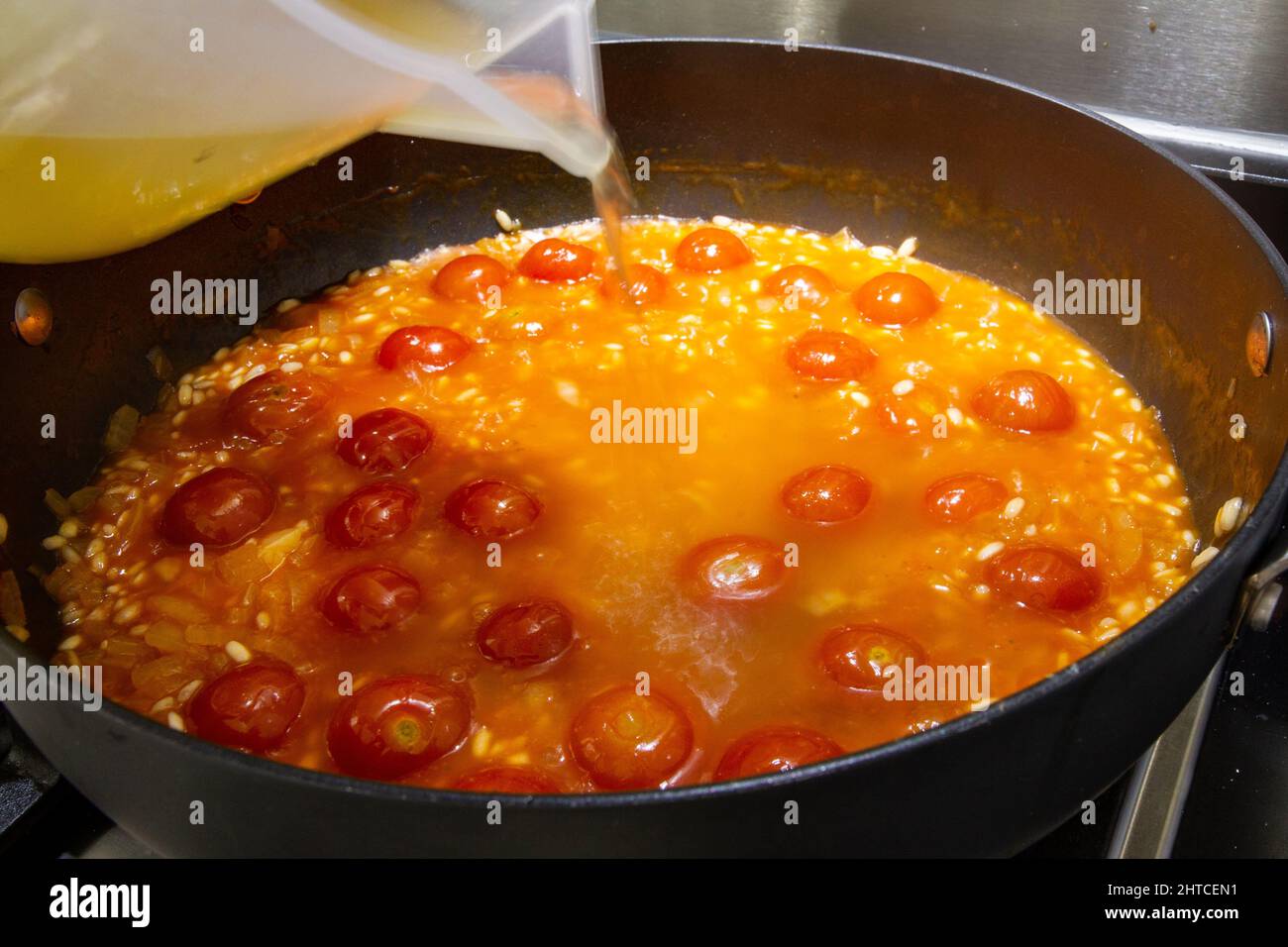 Adding stock to Tomato and mascarpone risotto Stock Photo - Alamy