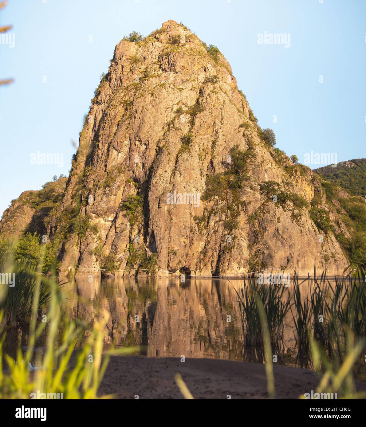 Beautiful view of a tall cliff with bushes and its reflection in the ...