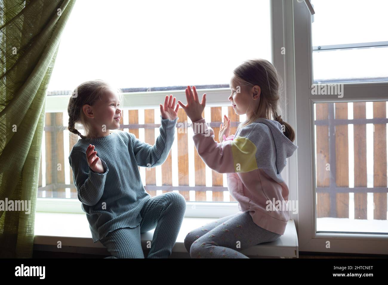 two girls are playing patty-cake, sitting on the windowsill near the ...