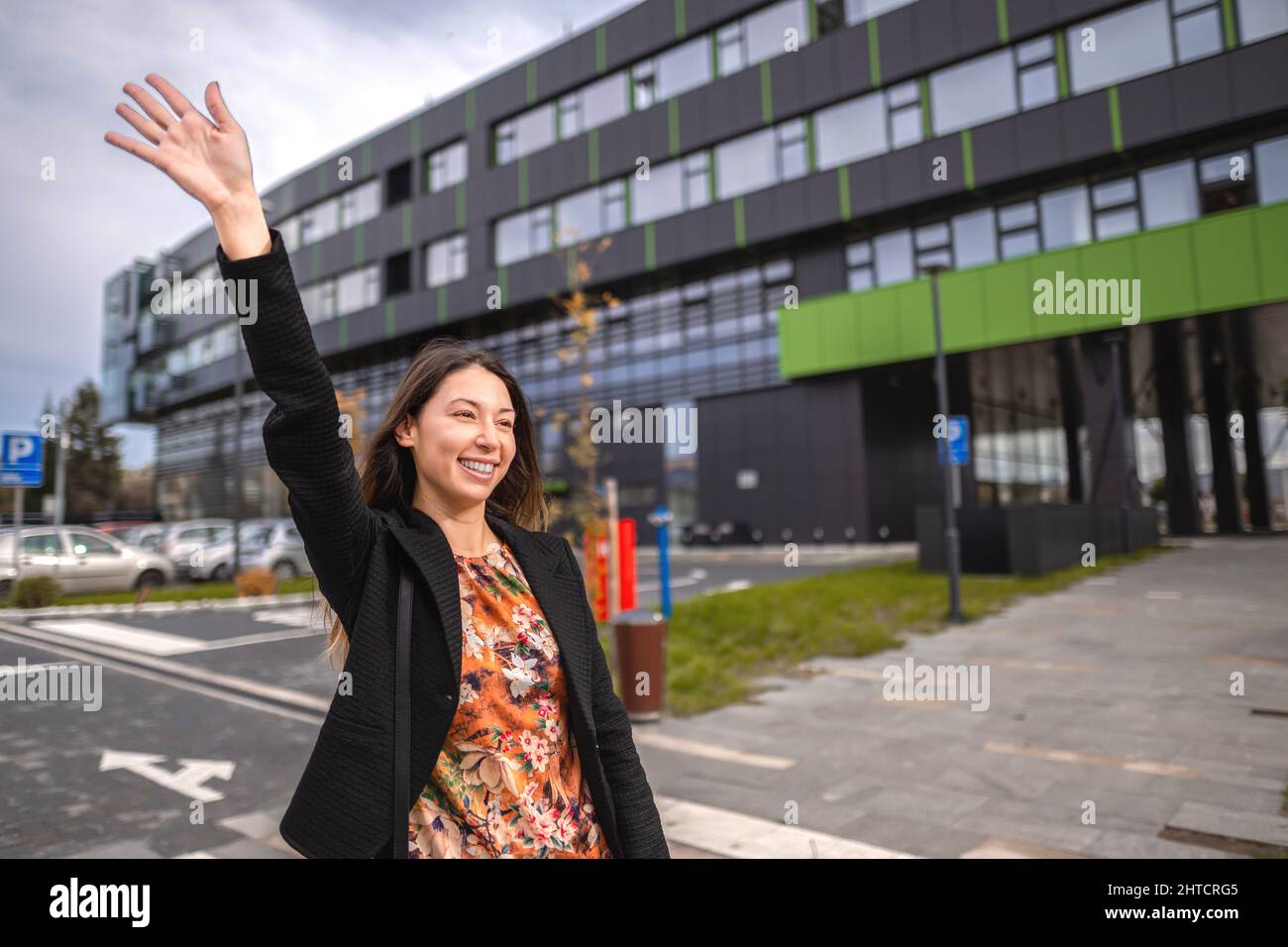 Young cheerful Caucasian lady greeting someone wearing a suit in front ...