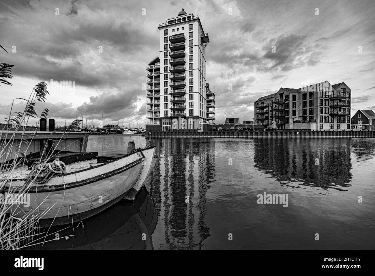Grayscale shot of a boat moored on the riverside with buildings ...