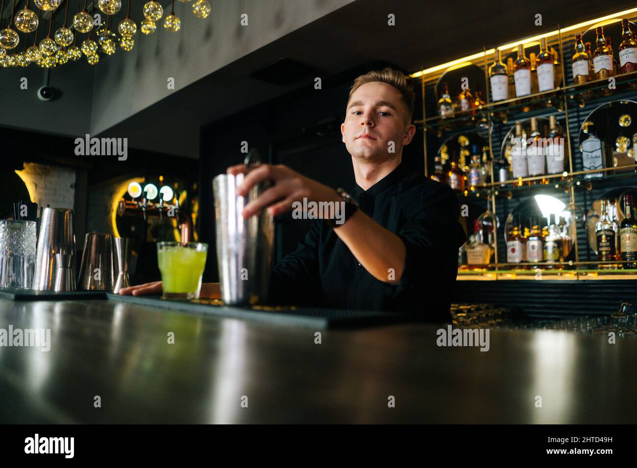 Low-angle view of young barman making colorful alcoholic cocktail ...