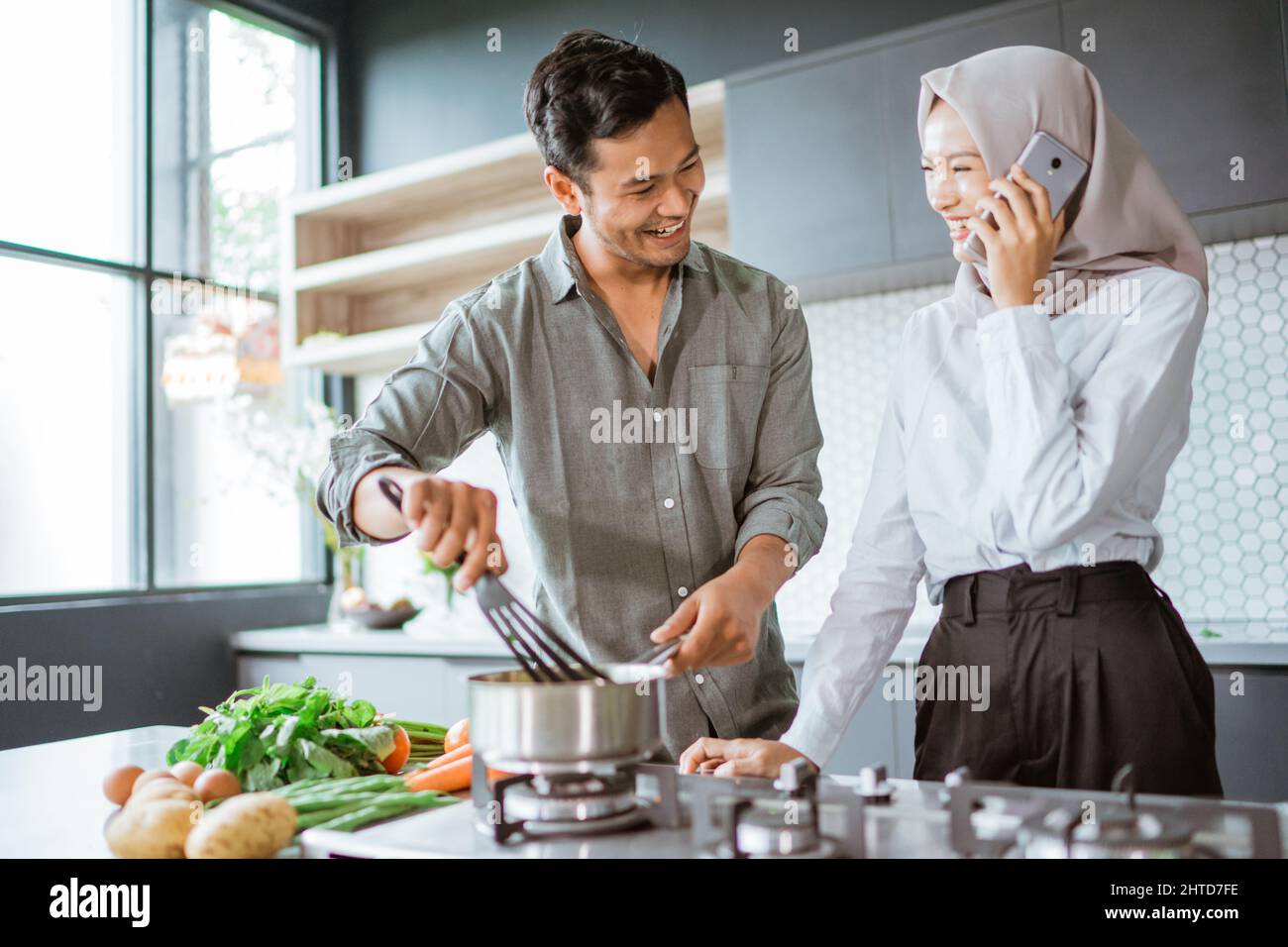 muslim couple cooking their food in the kitchen while wife taking a ...