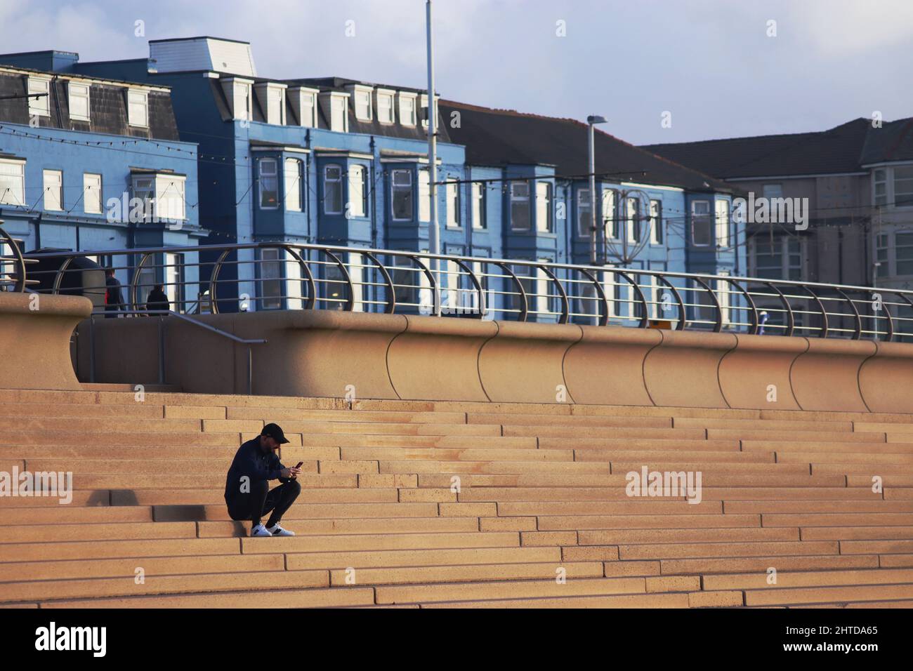 Young male watching something on this smartphone sitting on the stairs ...