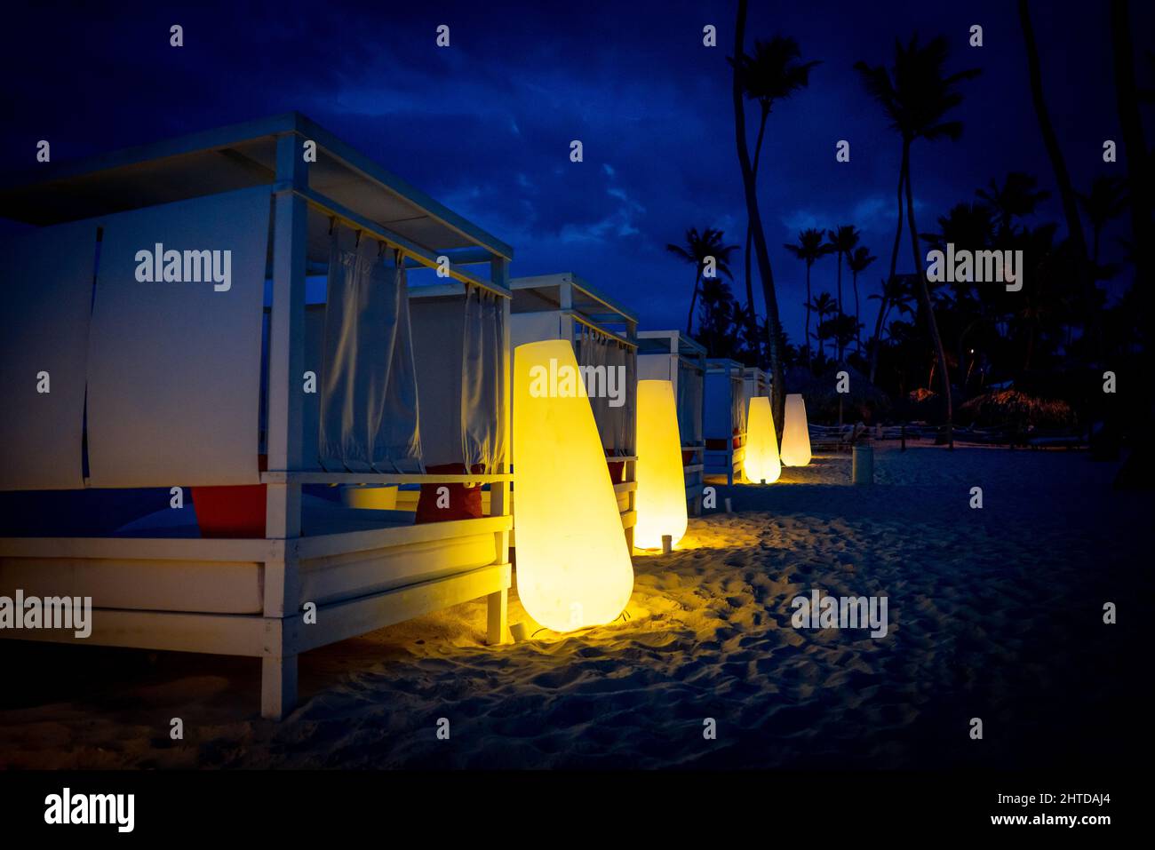 View of a sandy beach at night with white cabins for rest and palm ...