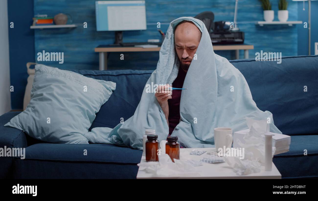 Ill man in blanket measuring temperature with thermometer to cure cold ...