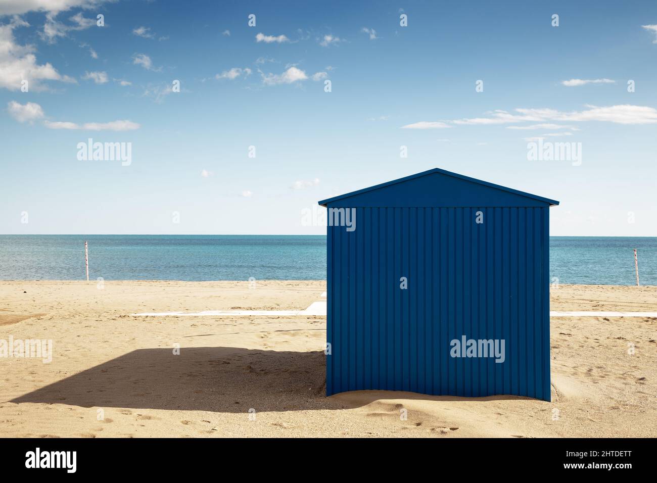 large blue shed on a sandy beach with the sea behind and a blue sky ...