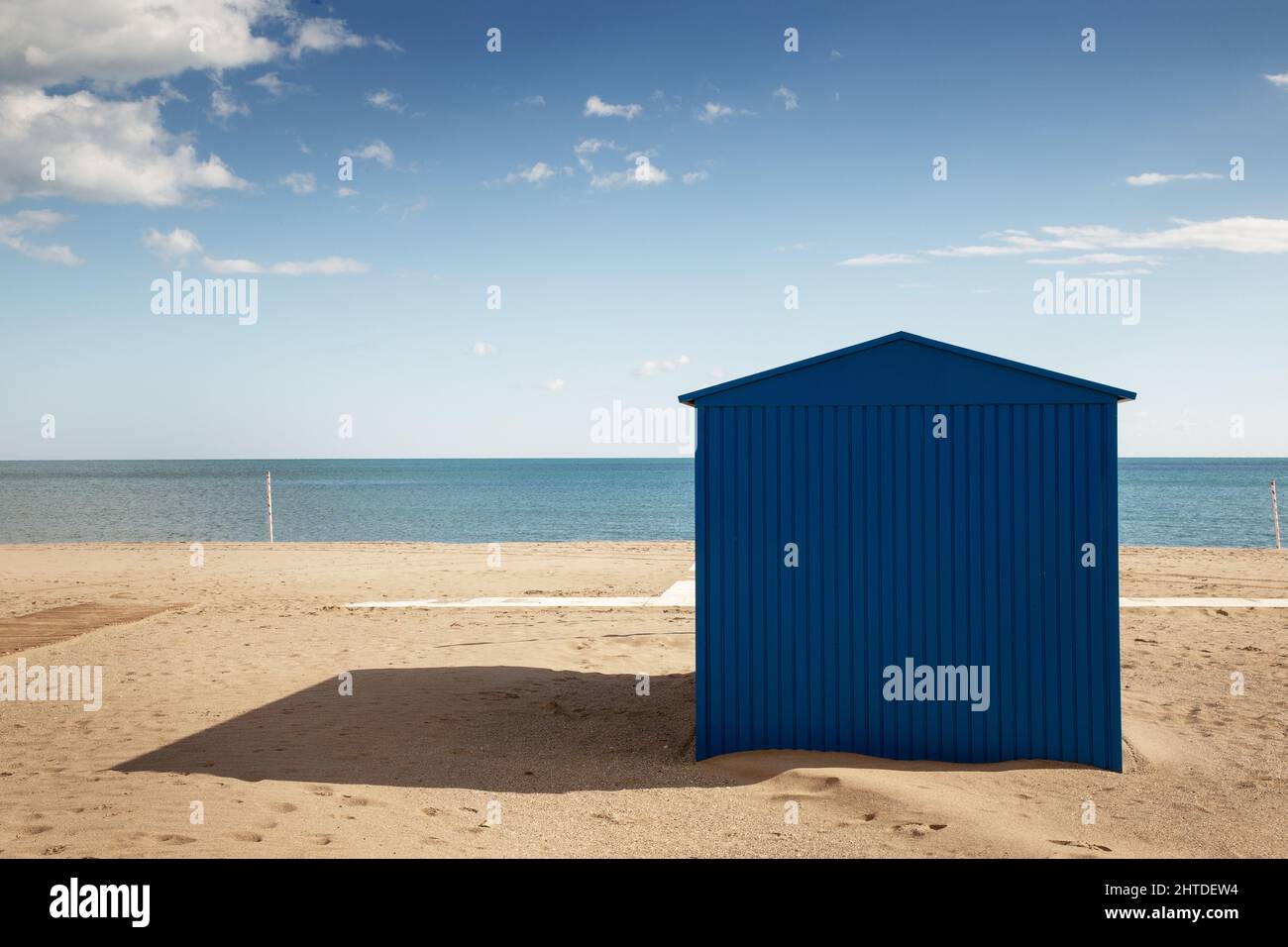 large blue shed on a sandy beach with the sea behind and a blue sky ...