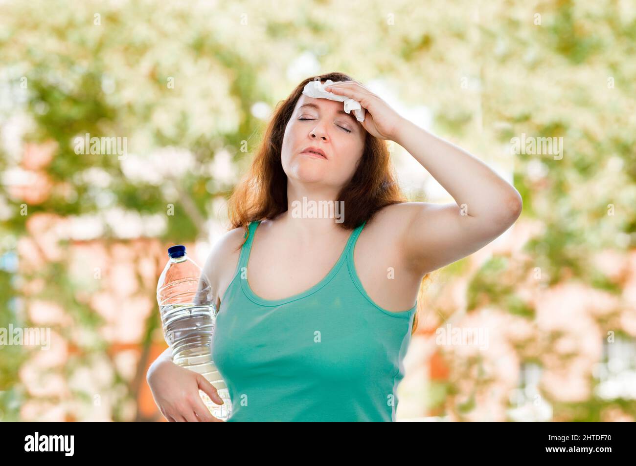woman sweating suffering a heat stroke with a bottle of water at park ...