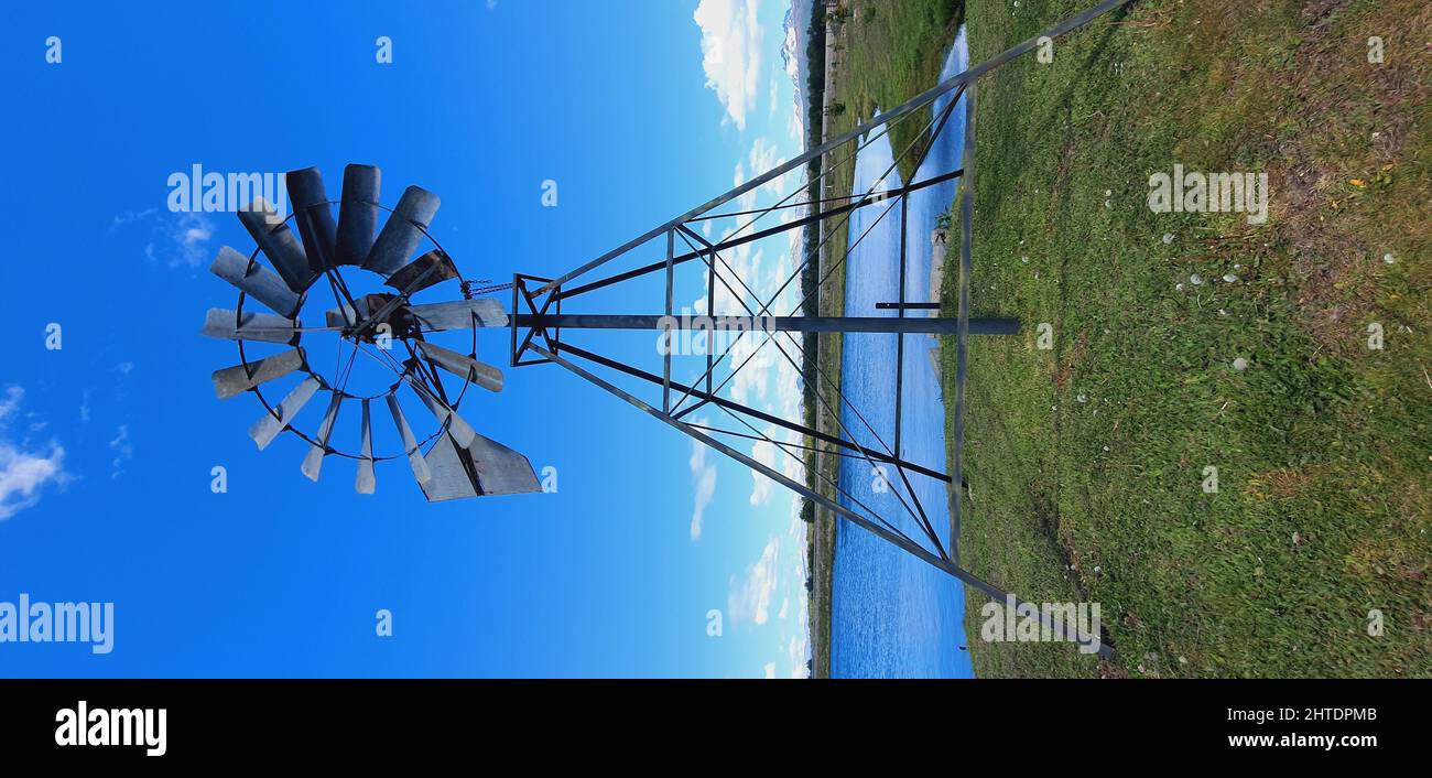 Vertical view of an old vintage windmill on a grass against a lake ...