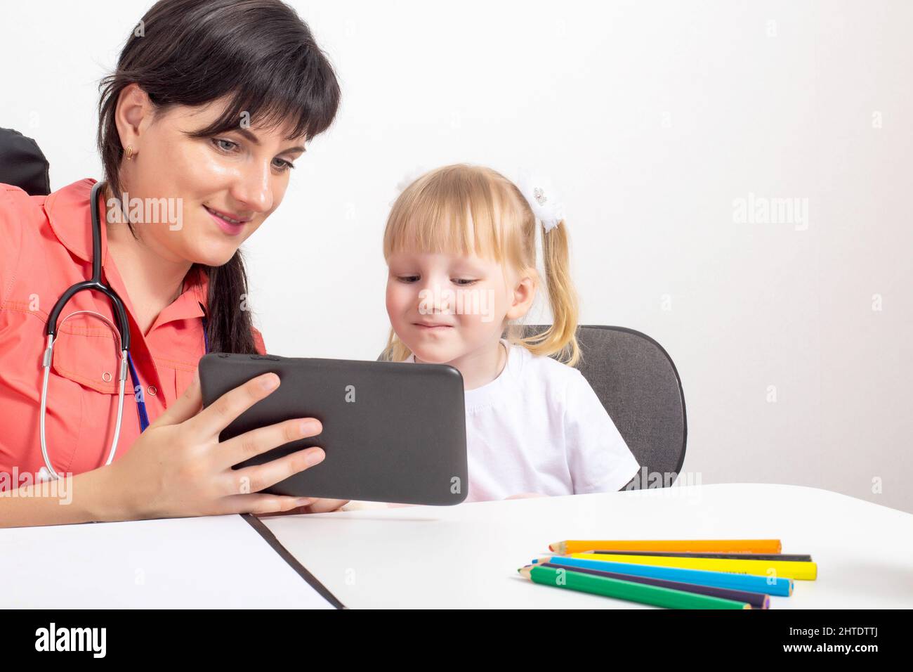 Doctor pediatrician shows a tablet to a little girl. Treatment of ...