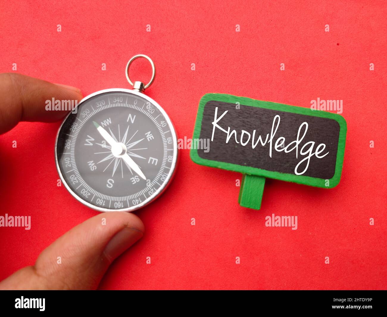 Hand holding compass near a board with text "Knowledge" on a pink ...