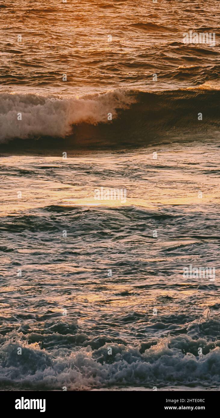 Vertical shot of a sea waves with a breathtaking sunset background ...