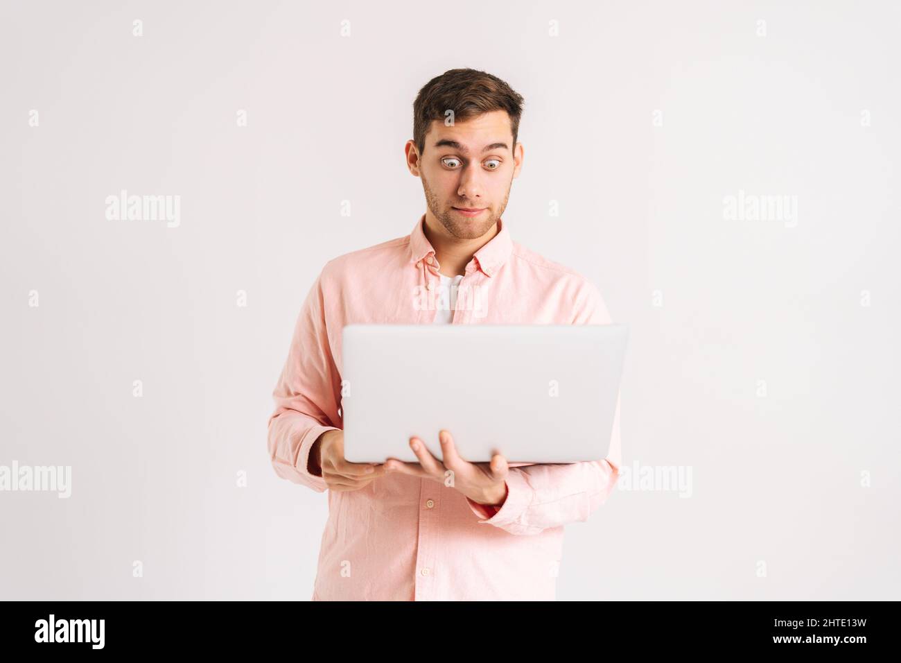 Portrait of shocked young man standing with laptop looking on screen ...