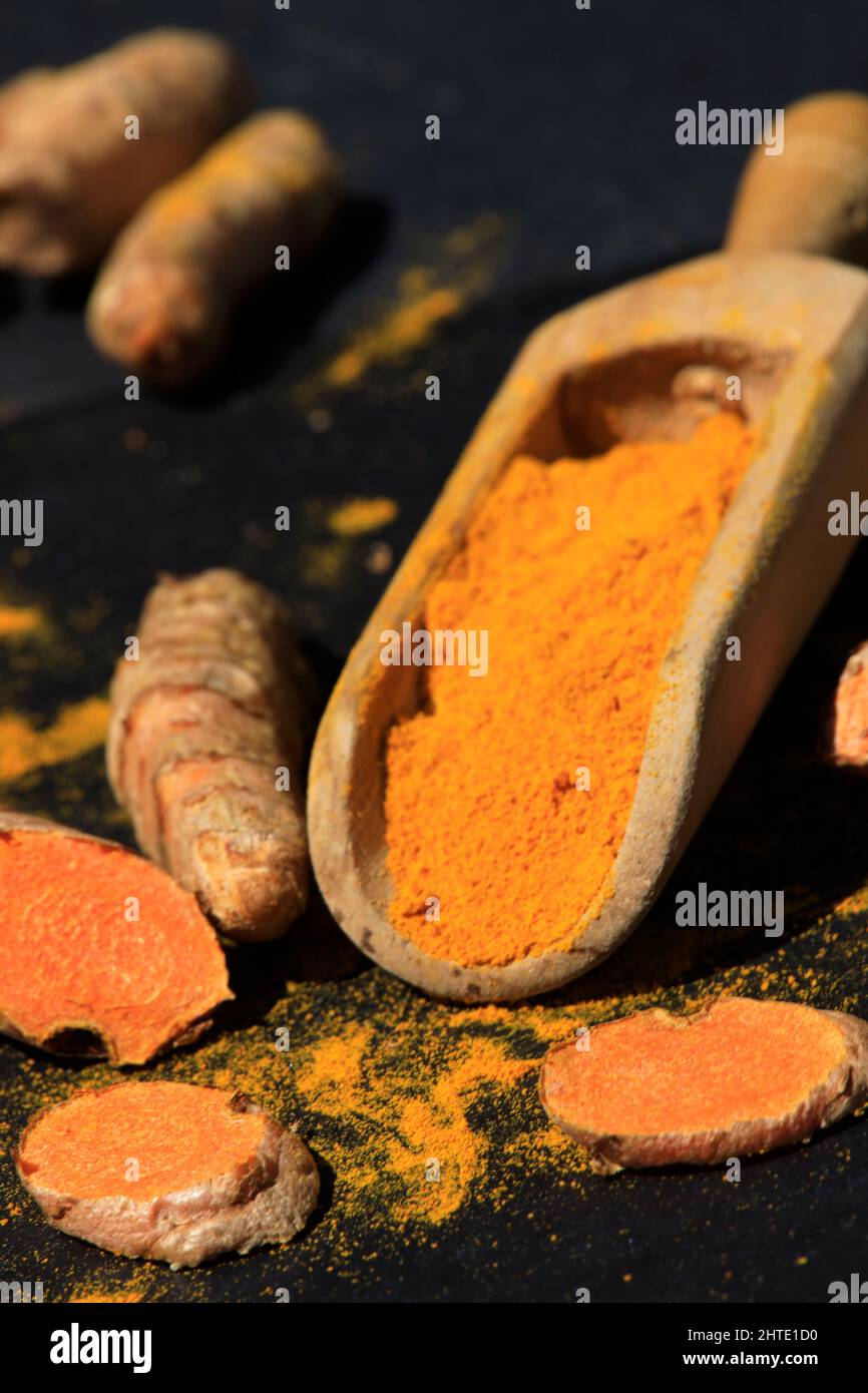 Turmeric powder (Kurkuma) in a wooden spoon and roots on a dark table ...