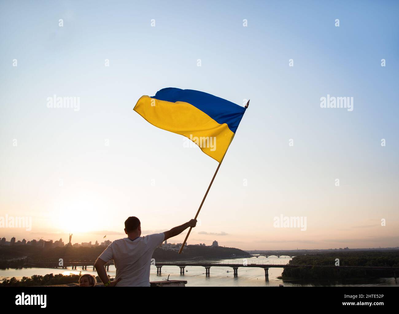 Ukrainian flag flutters in the wind against the sunset sky. A man ...