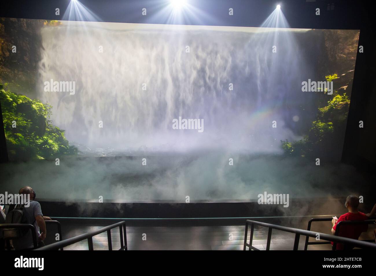 Display of waterfall on a screen and people standing and looking at it ...