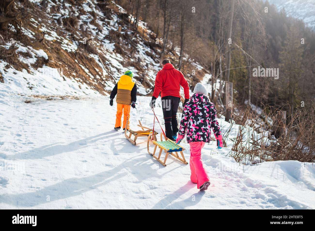 Father, daughter, and son going uphill on a snow slope and pulling ...
