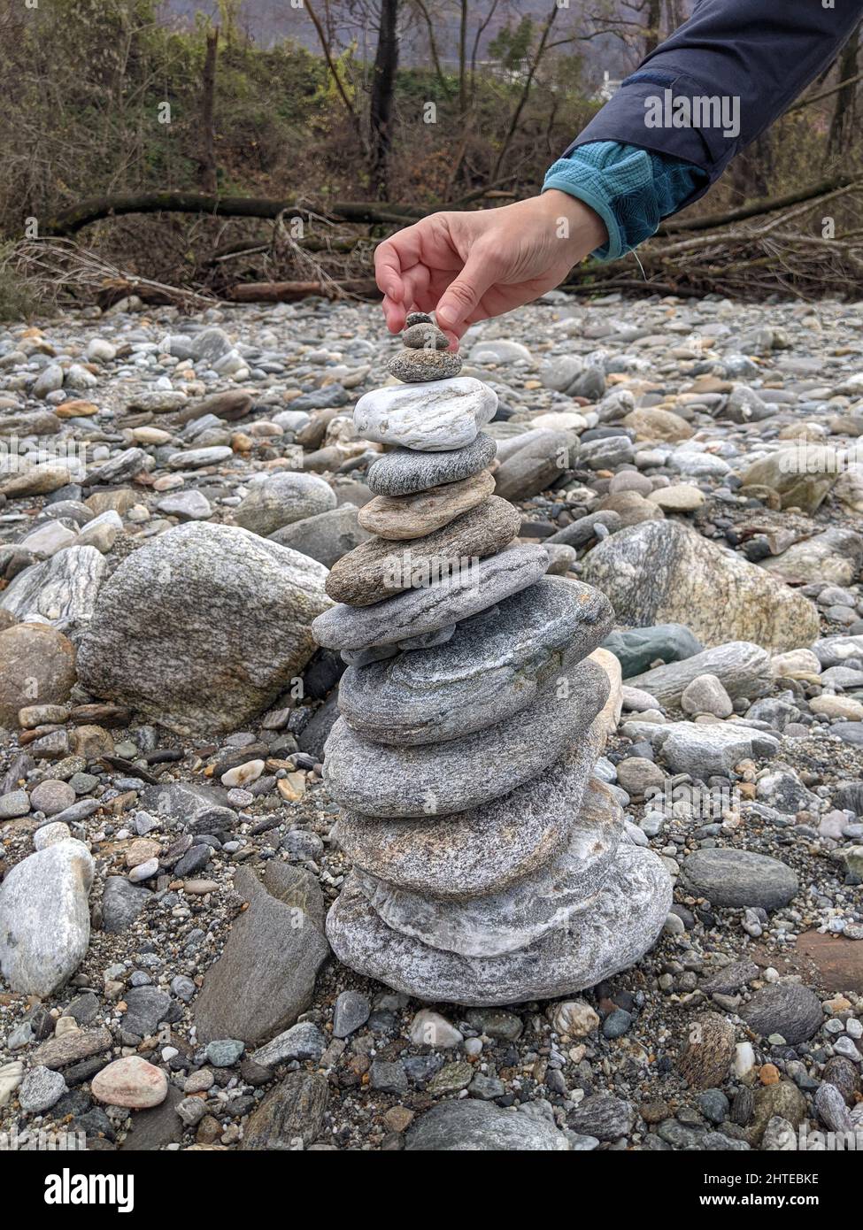 Vertical closeup of a hand putting pebbles on one another on a rocky ...