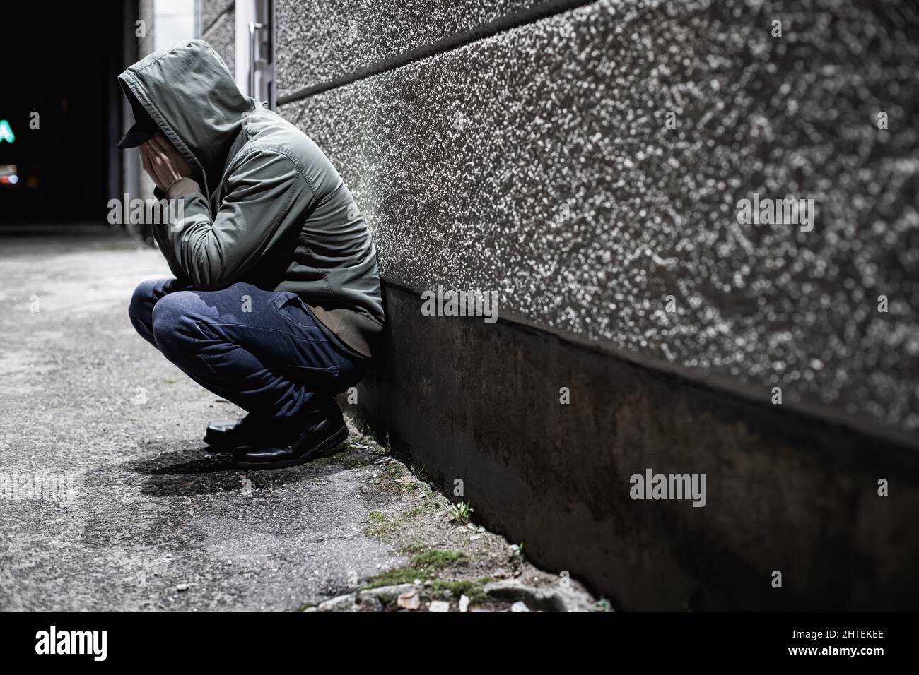 Lonely man in a jacket sitting on a street while covering his face ...