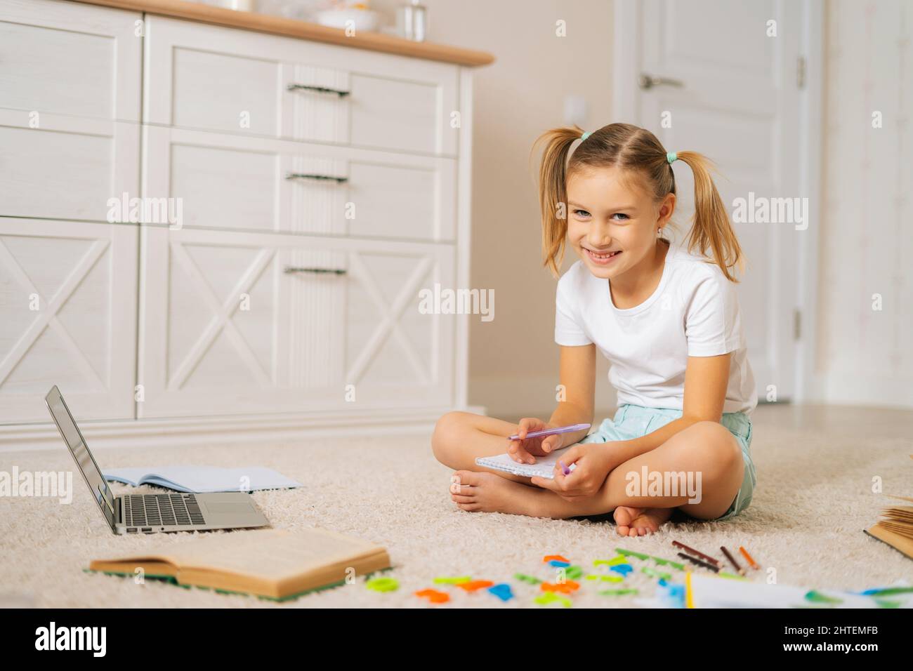 Portrait of cheerful primary girl child writing homework in notebook ...