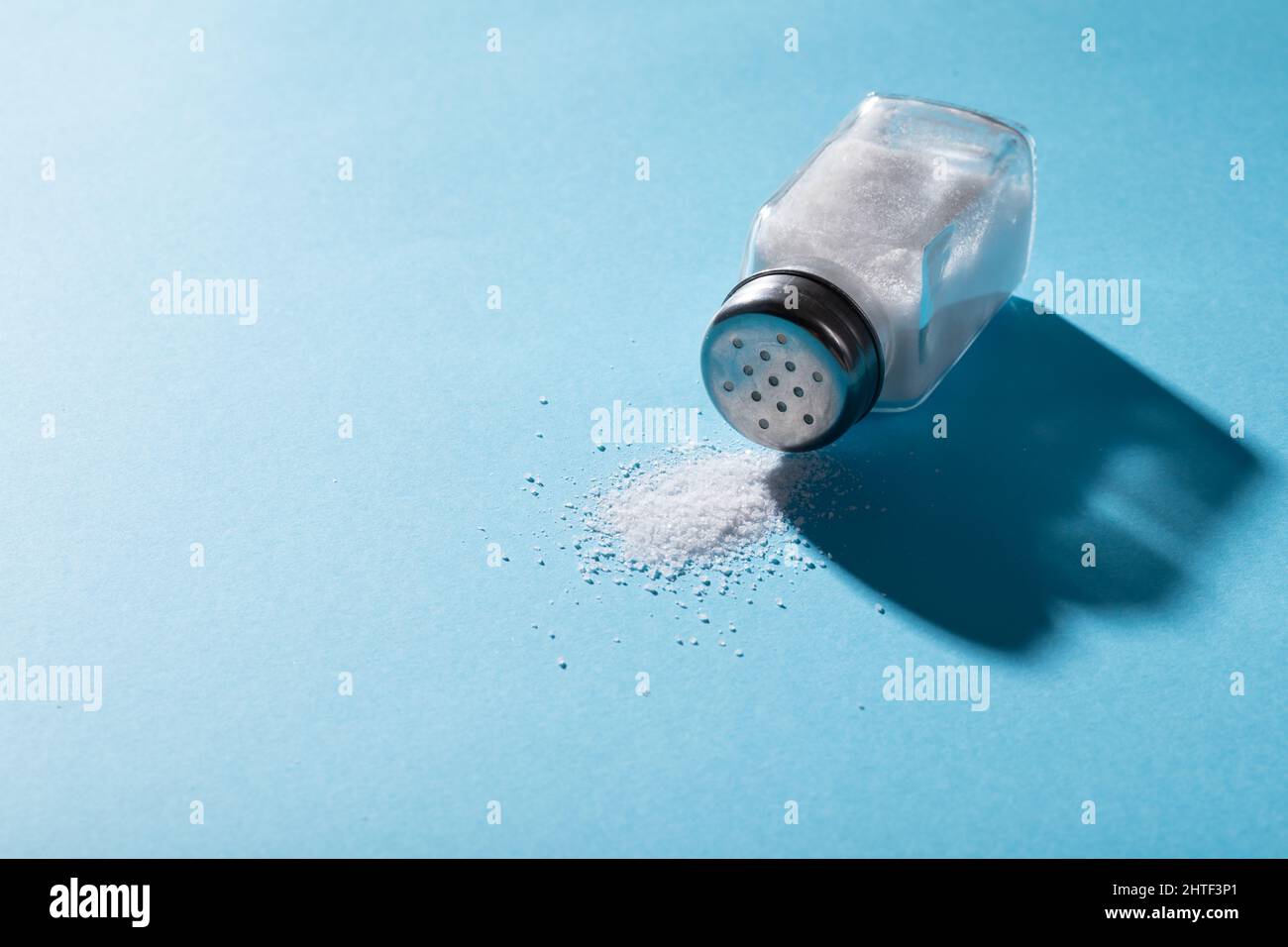 High angle close-up of salt spilling from salt shaker on blue ...