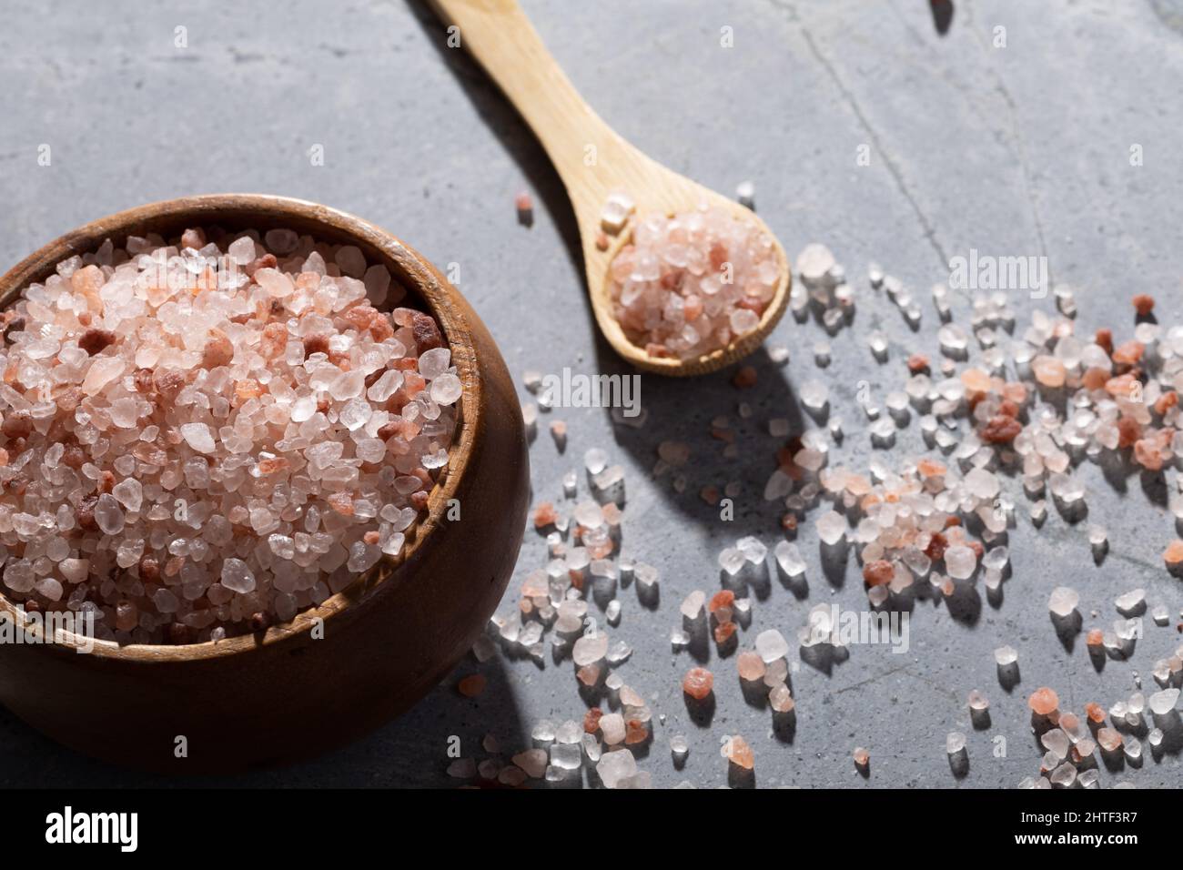 Light falling over pink rock salt in wooden bowl and spoon on table ...