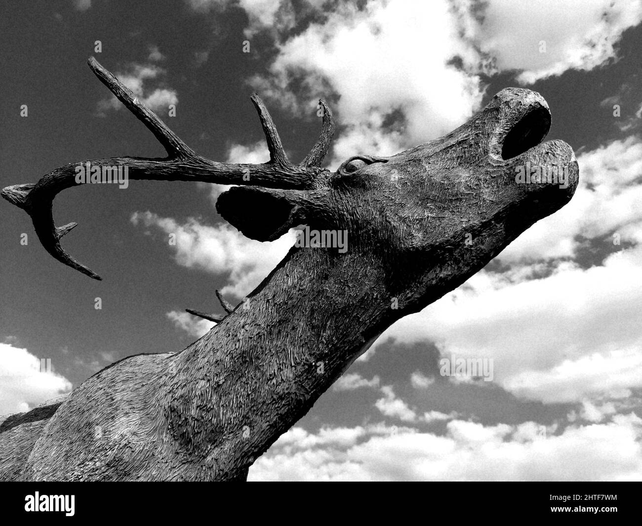 Grayscale bottom shot of a deer sculpture in the background of a cloudy ...