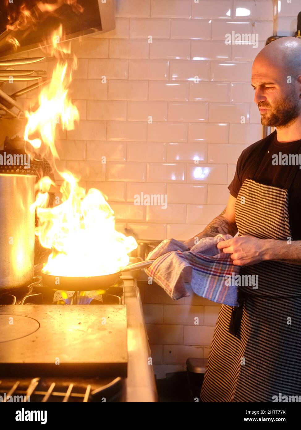 Cook flaming the food in a pan in a restaurant kitchen Stock Photo - Alamy