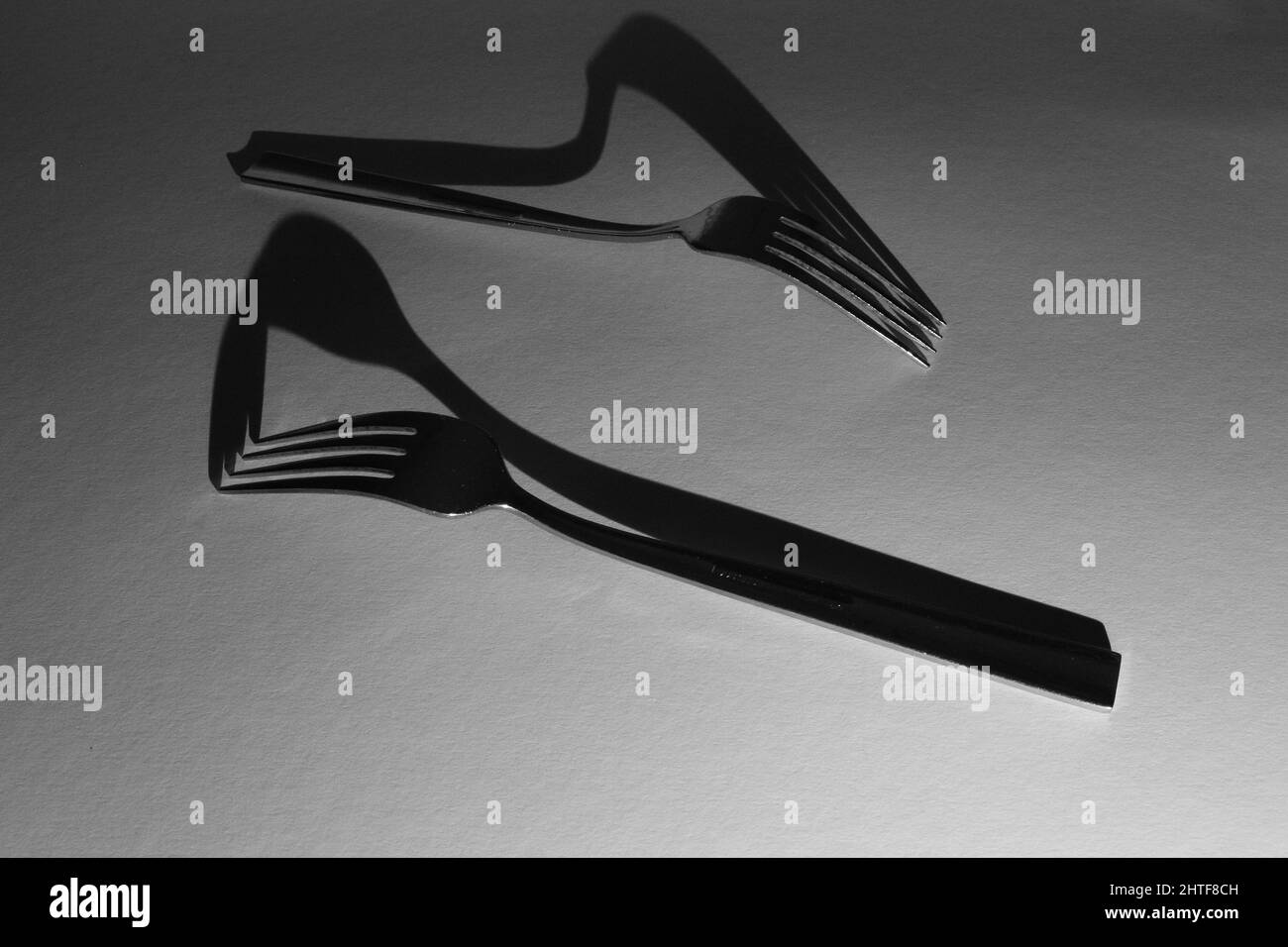 Closeup grayscale of the metal forks with their shadows on the shiny ...