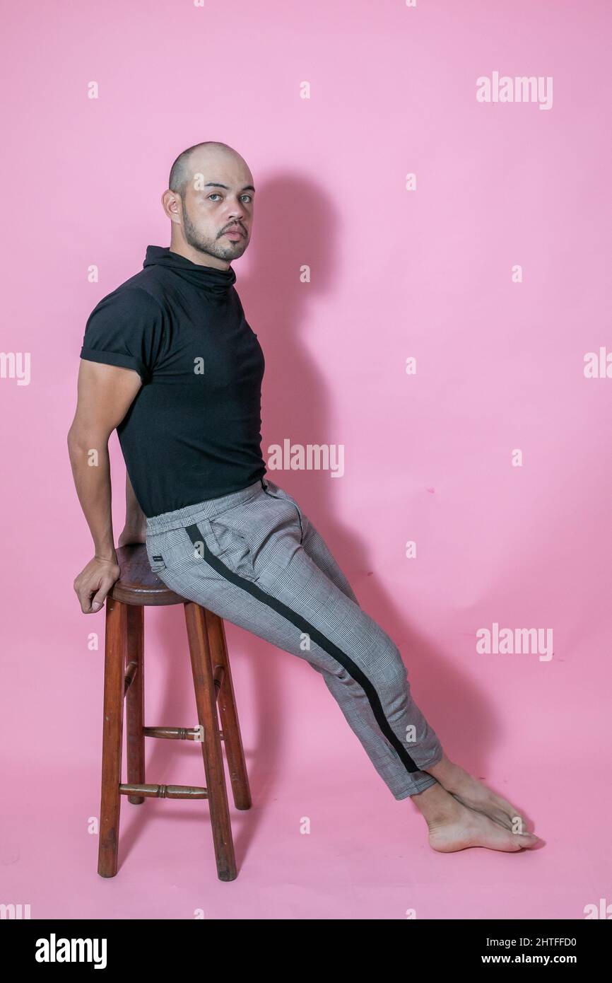 Full body shot of a young handsome bald Mexican man sitting on a chair ...