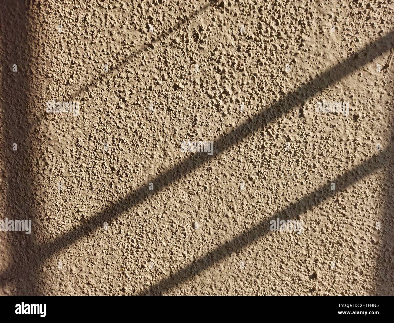 Painted wall with a rough grungy texture and shadows of bars falling on ...