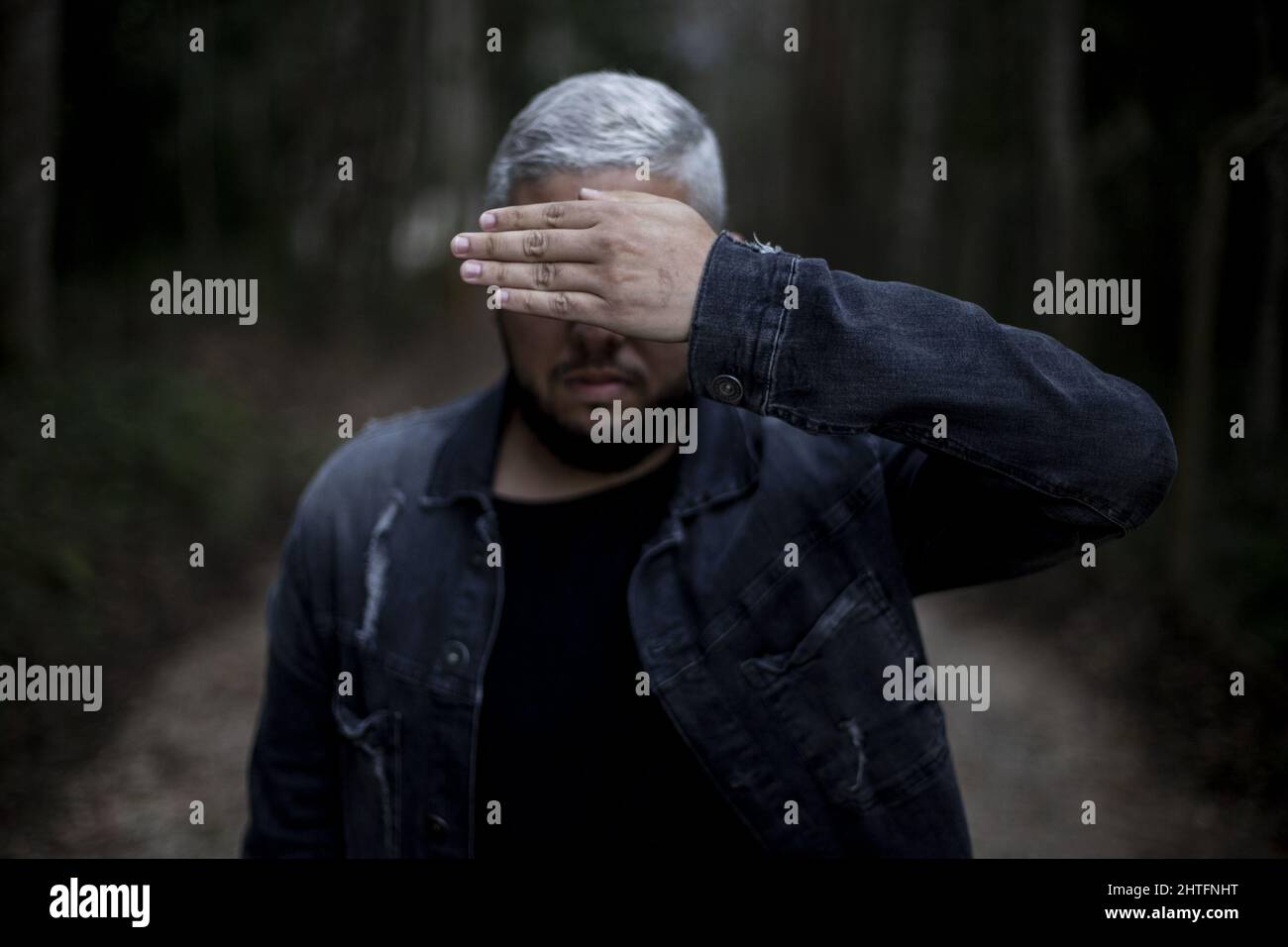 Man with gray hair in a denim jacket covering his face with hand Stock ...