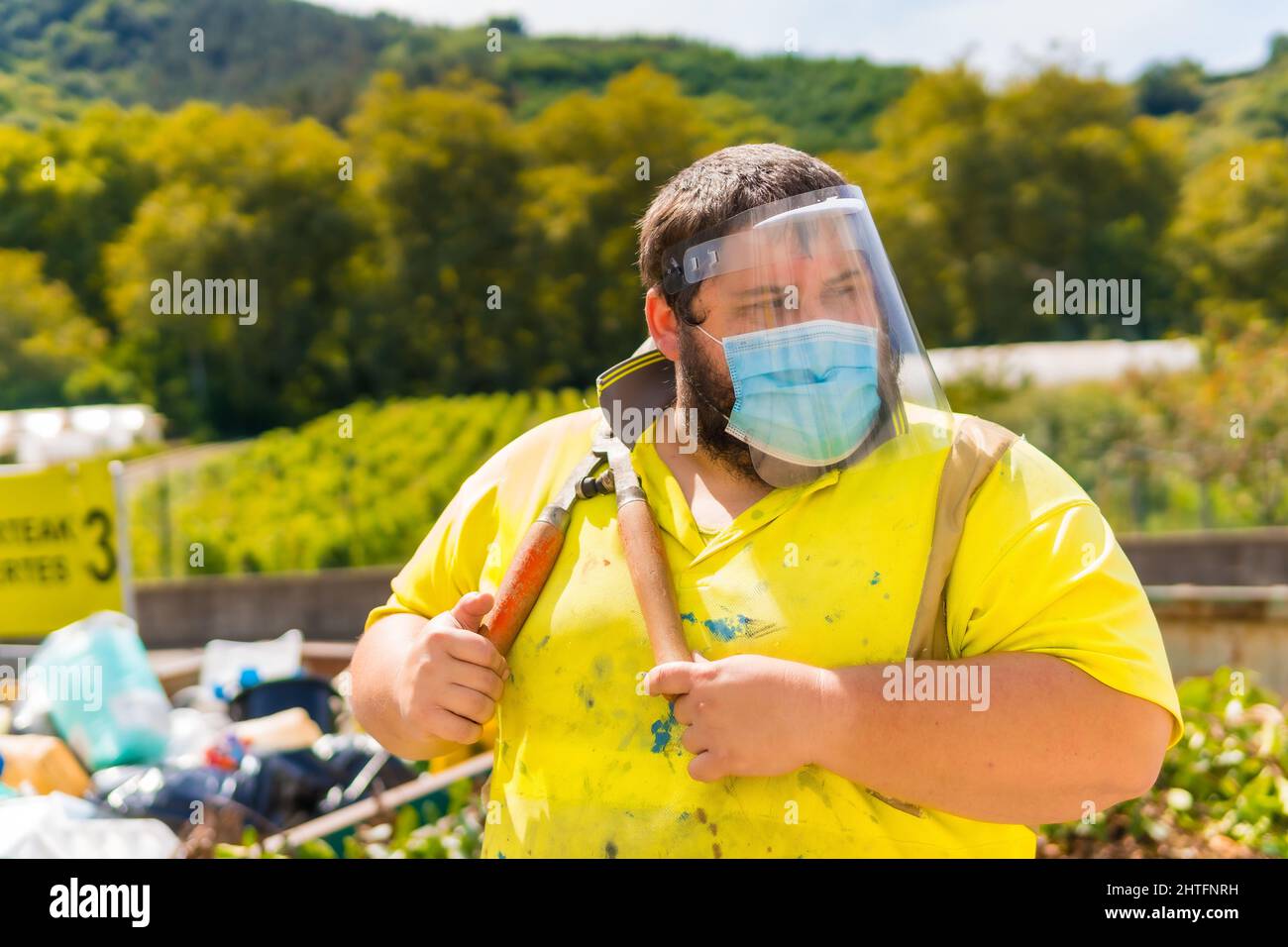 A cleaner with a bush clipper wearing a protective face shield and mask ...