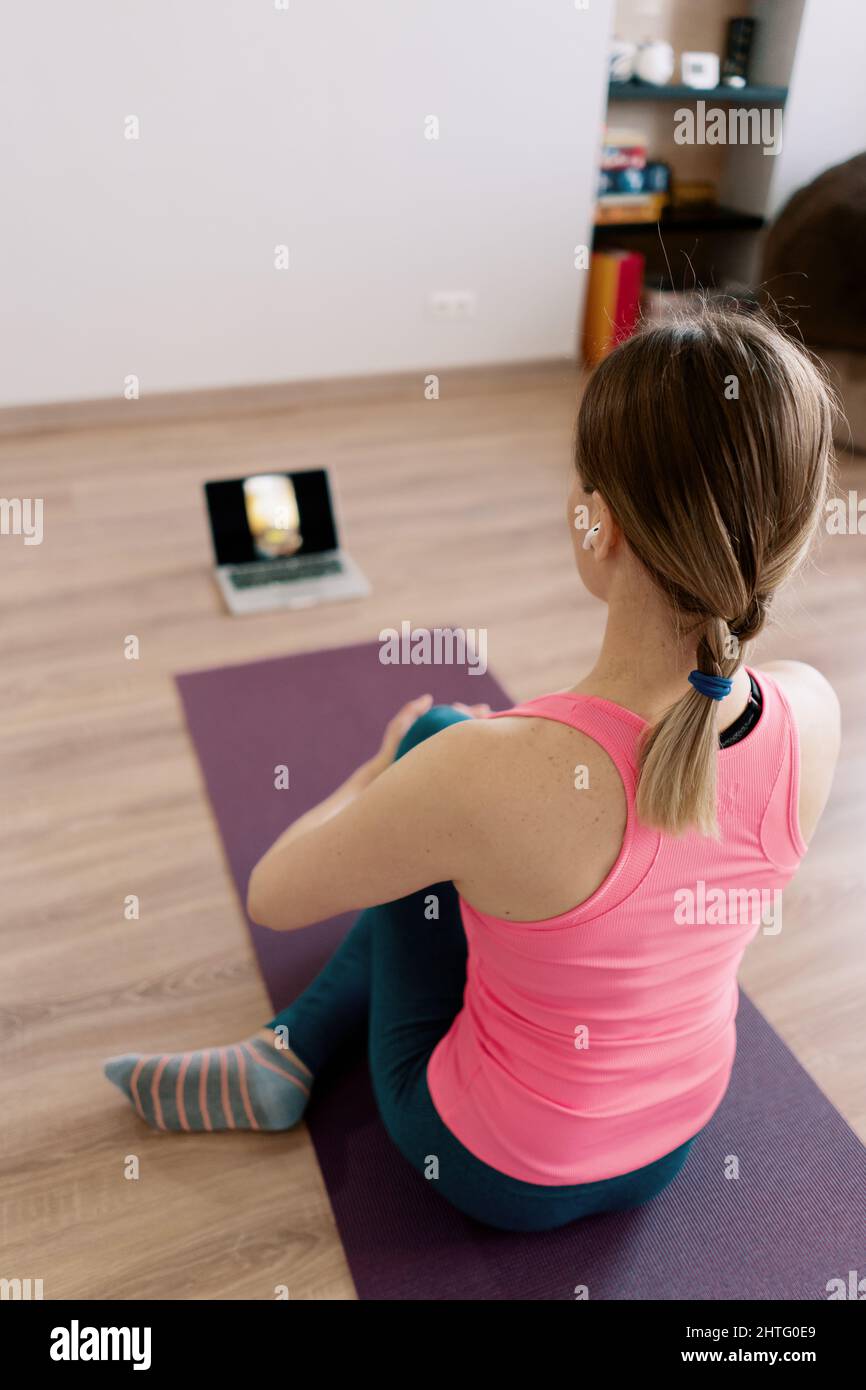 Back view authentic woman practicing yoga at home using online training ...