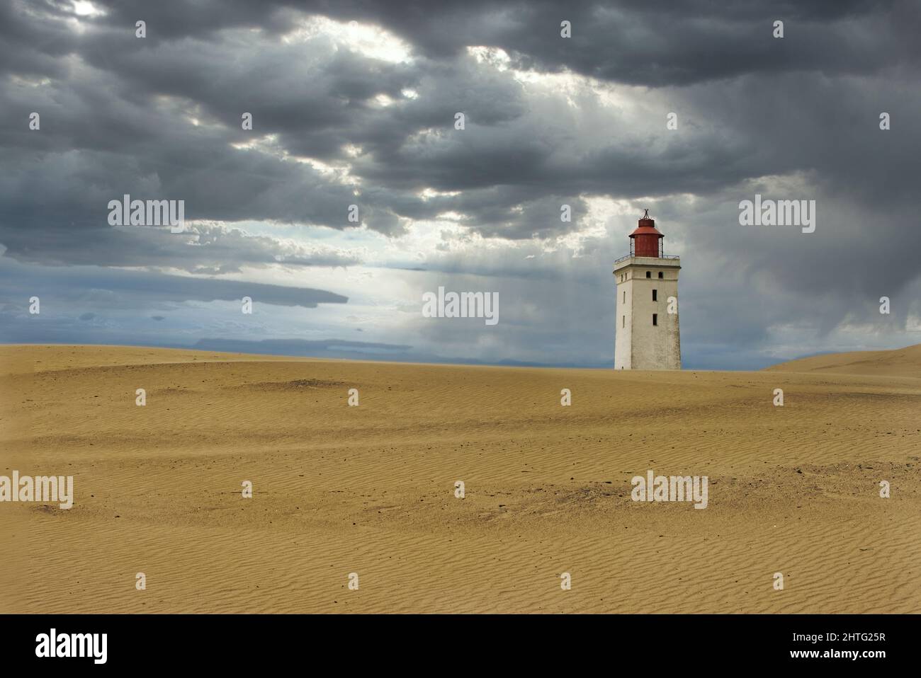 Lighthouse on a sand dune on background of gloomy clouds Stock Photo ...