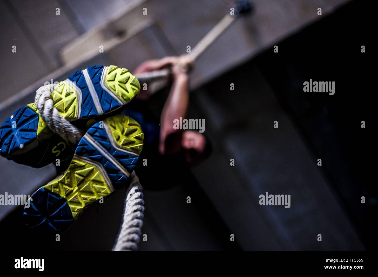 Low angle shot of feet of a person climbing a rope in a sports center ...