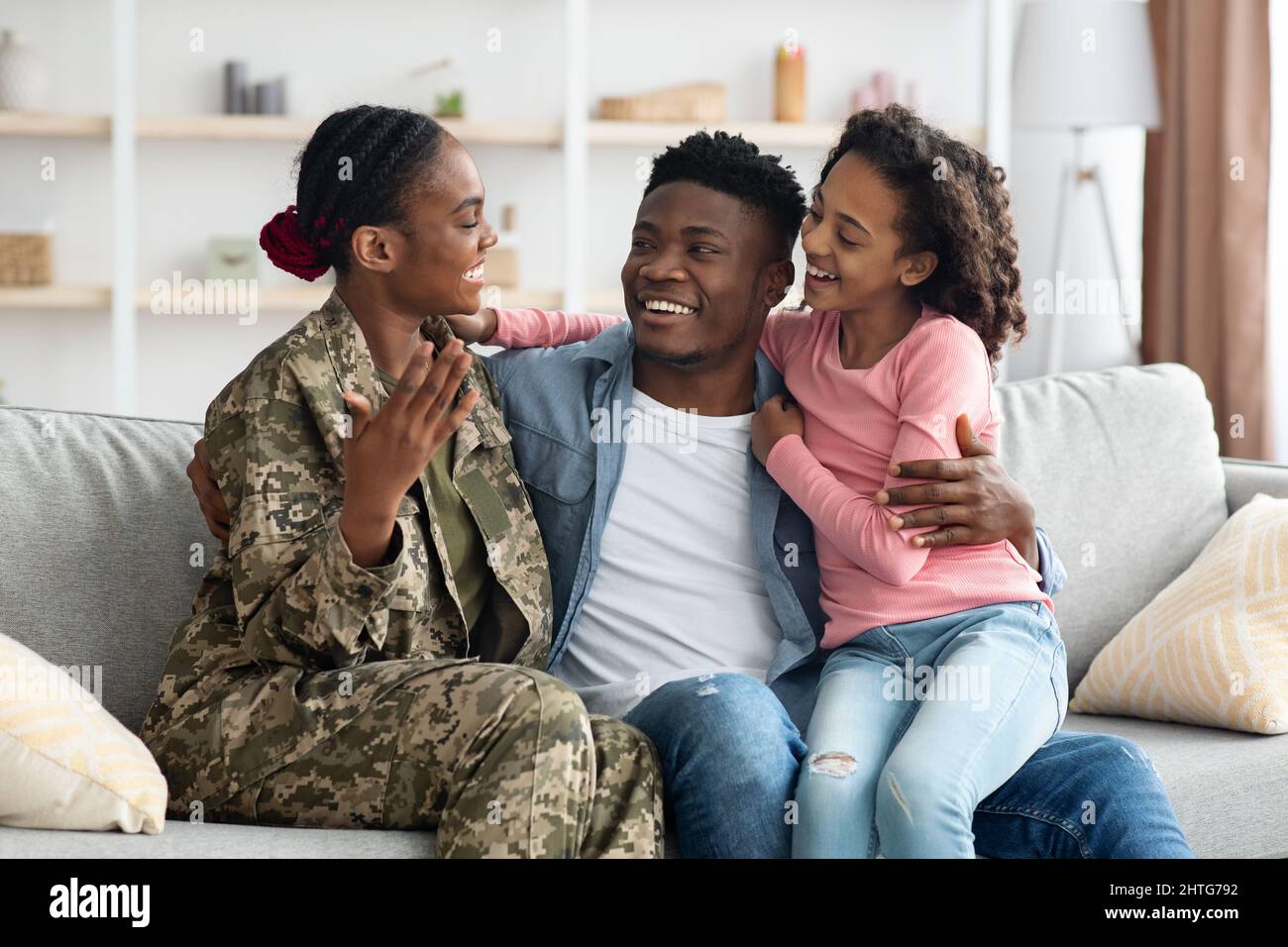 Cheerful family sitting on couch, mother soldier back from service ...