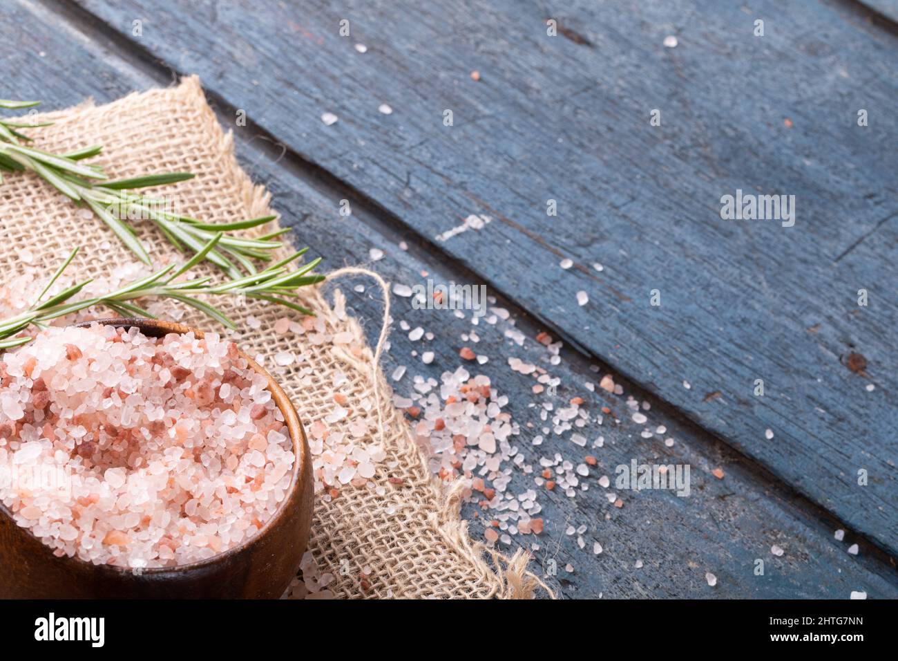 Close-up of pink rock salt in bowl by rosemary on jute fabric at table ...
