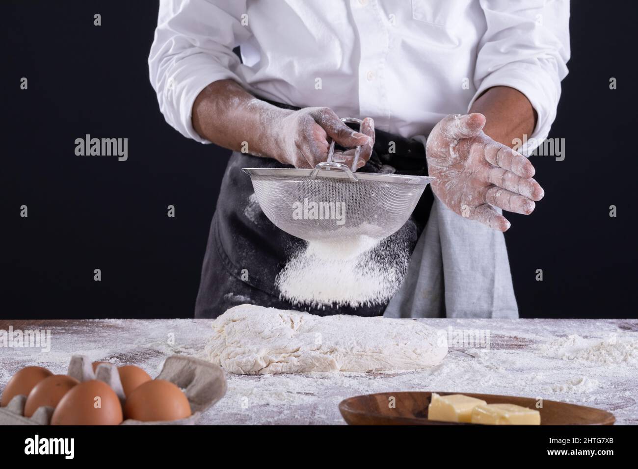 Midsection of african american male baker sieving flour on dough while ...