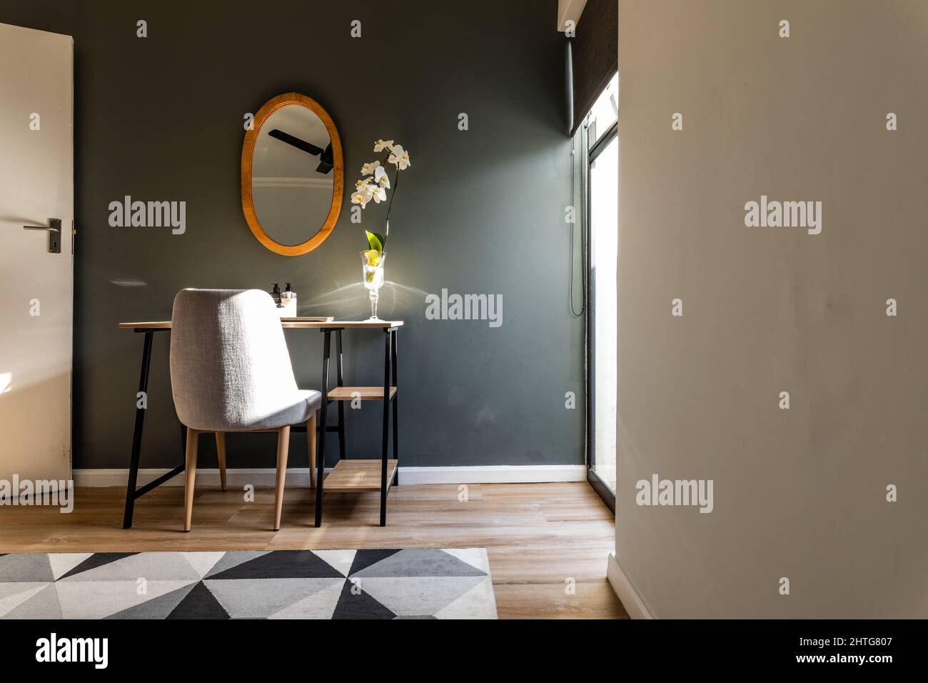 Chair at table below mirror in bedroom at home during sunny day, copy ...