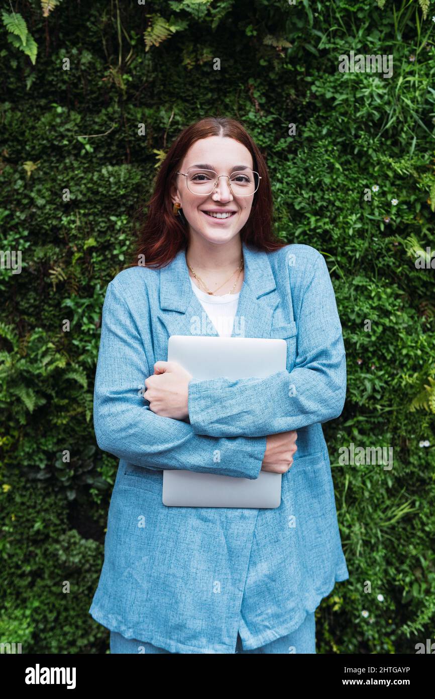 Confident businesswoman holding laptop and smiling at camera Stock ...